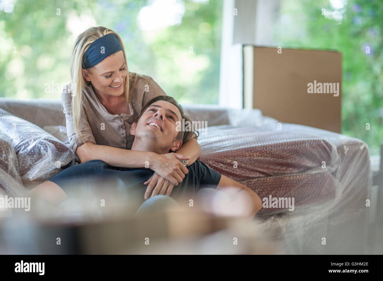 Moving house: woman sitting on bubble wrapped sofa, arms around man's ...