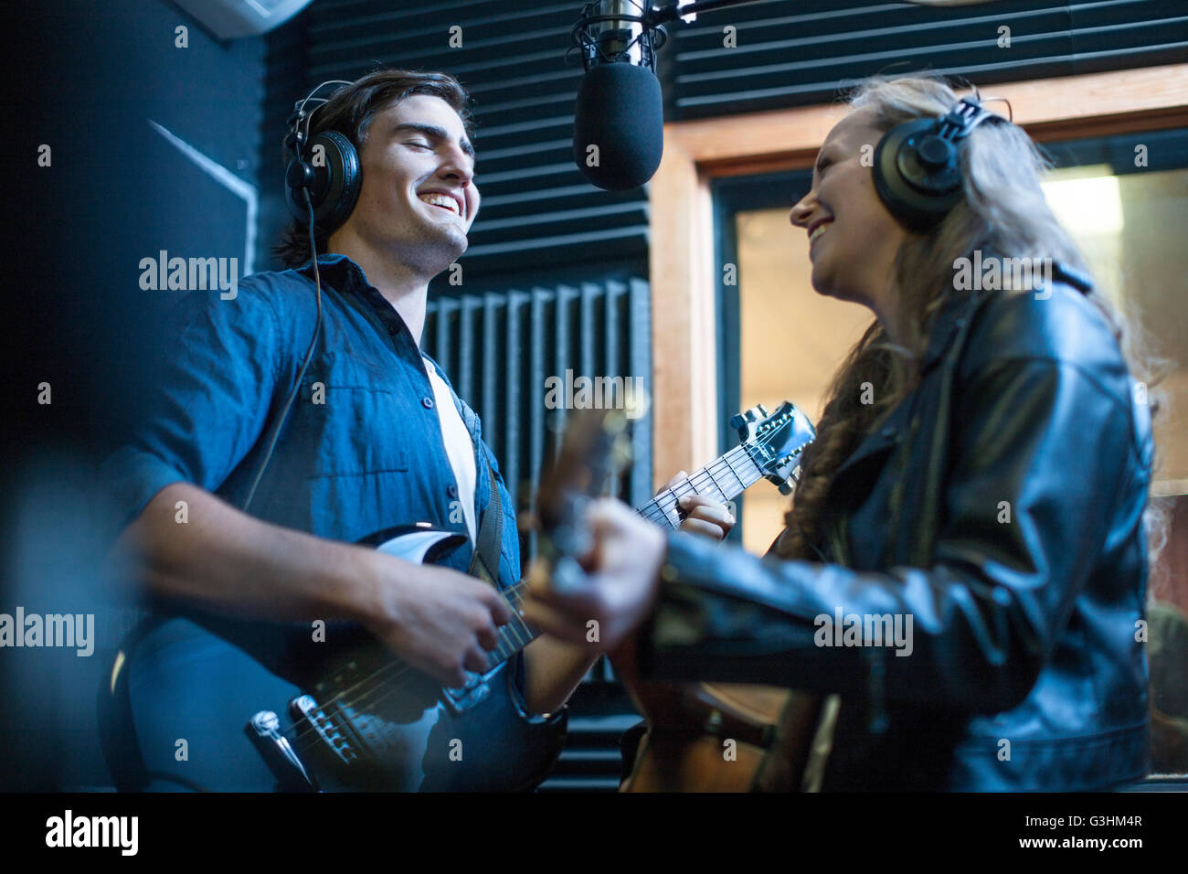 Two musicians in recording studio, singing into microphone and playing ...