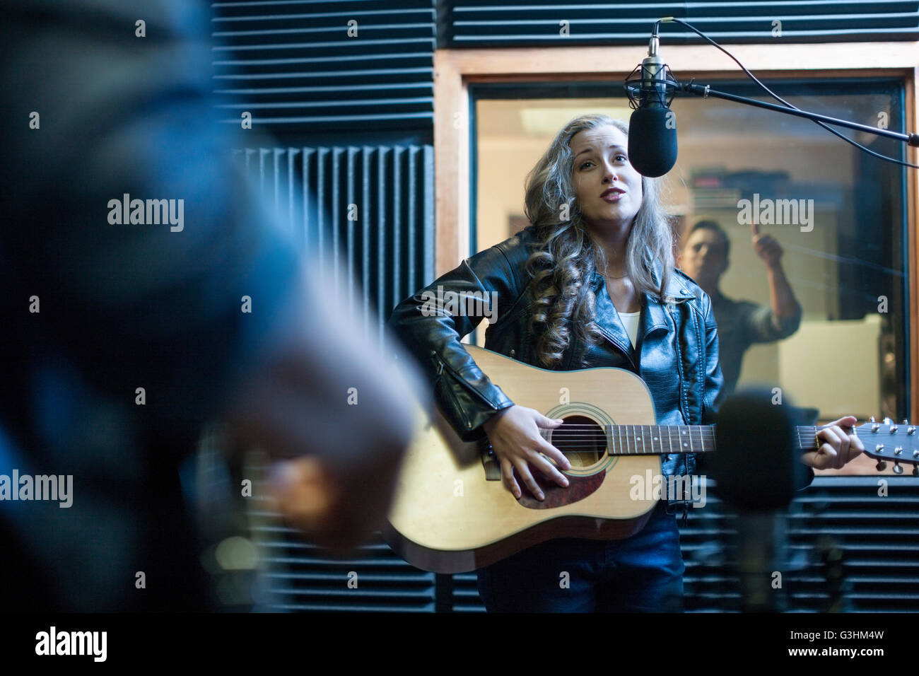 Two musicians in recording studio, singing into microphone and playing ...