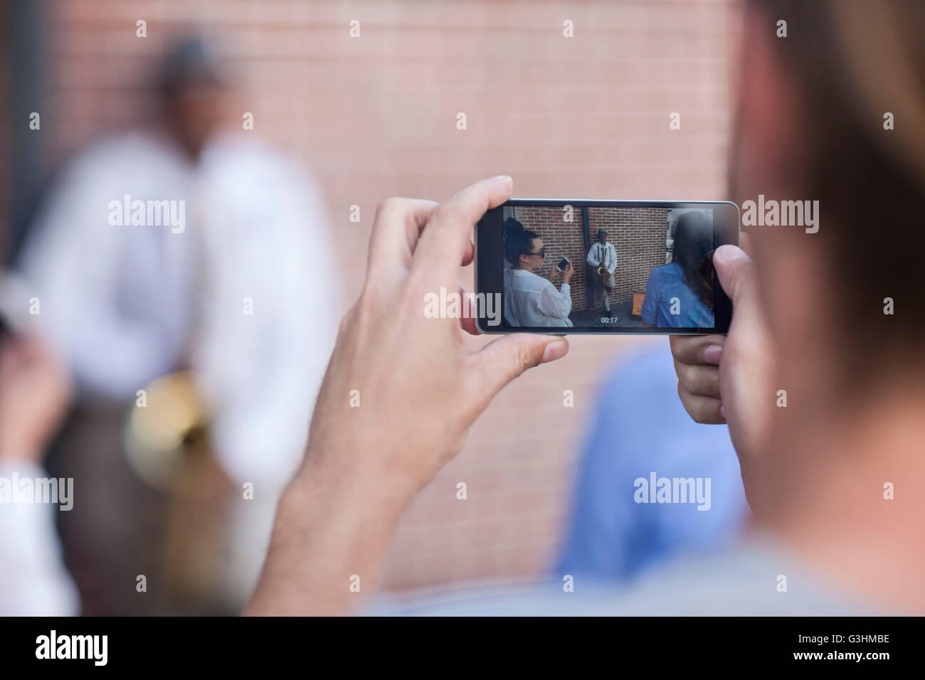 Pedestrian taking photograph of street musician, using smart phone ...