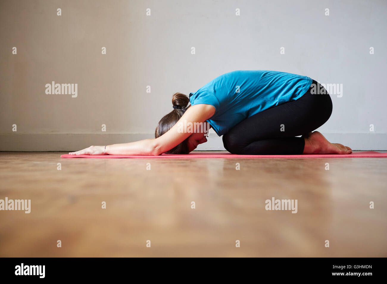 Side view of woman bending forward, hands on floor in yoga position ...
