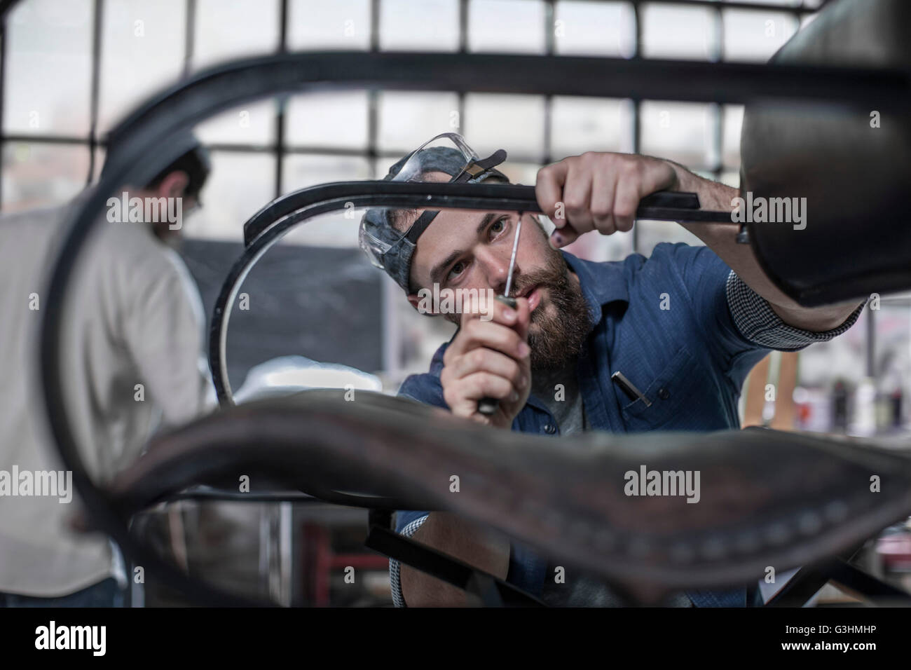 Young craftsman using screwdriver on chair in antique restoration ...