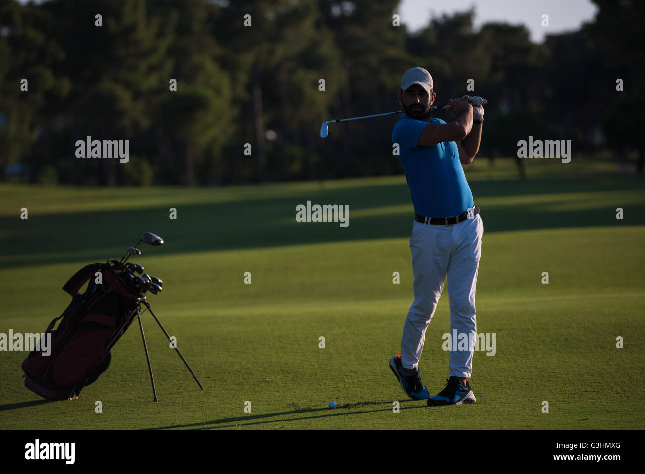 golfer hitting long shot with driver on course at beautiful sunset ...