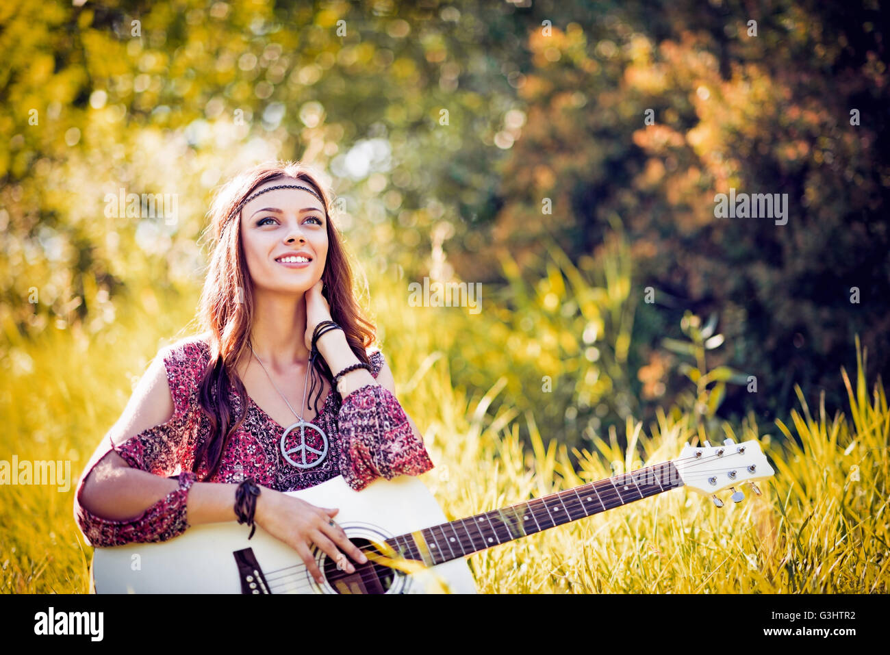 Portrait of a beautiful smiling hippie girl with guitar. Outdoor shot ...