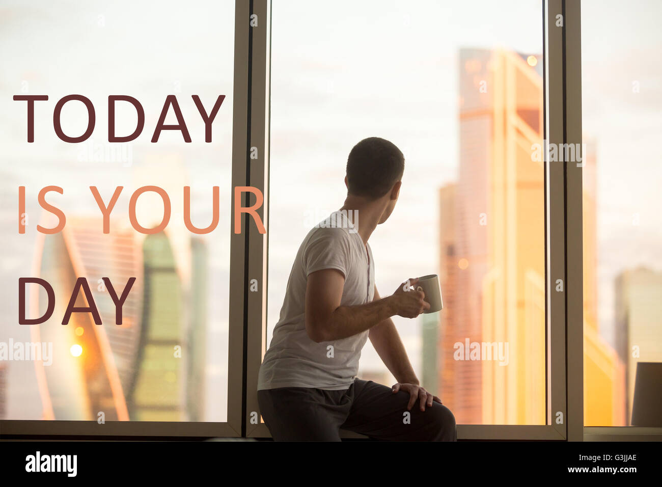 Rear view of young man sitting on window with coffee cup looking at ...