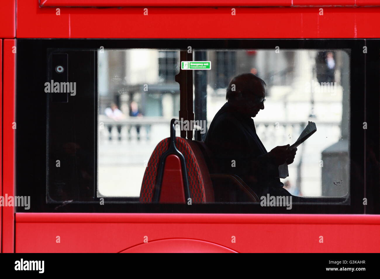 A view of a male reading a newspaper while sitting inside a red London ...