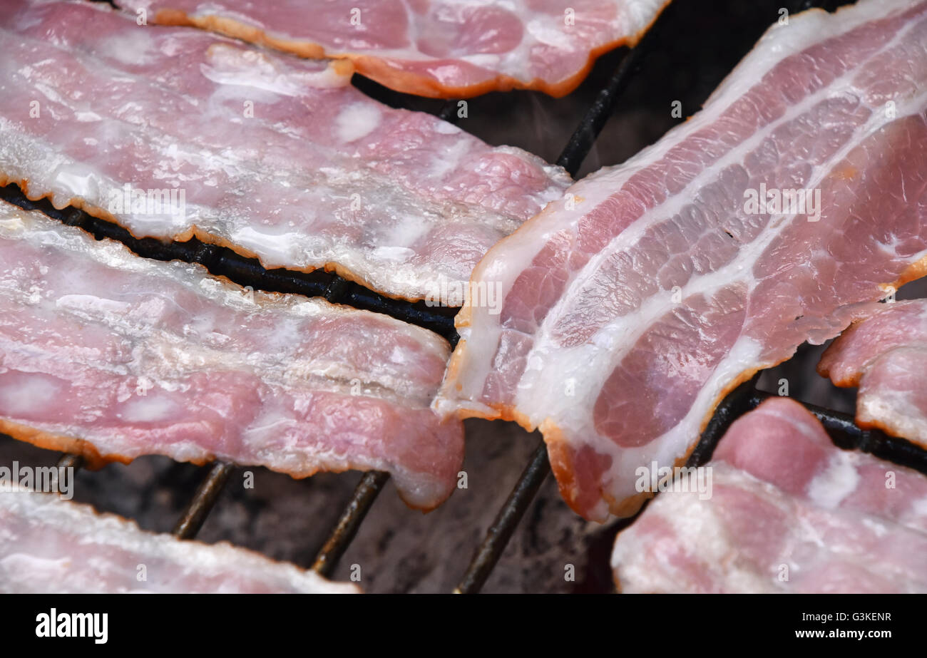 Raw smoked melting grilled barbecue bacon slices, being cooked on bbq ...
