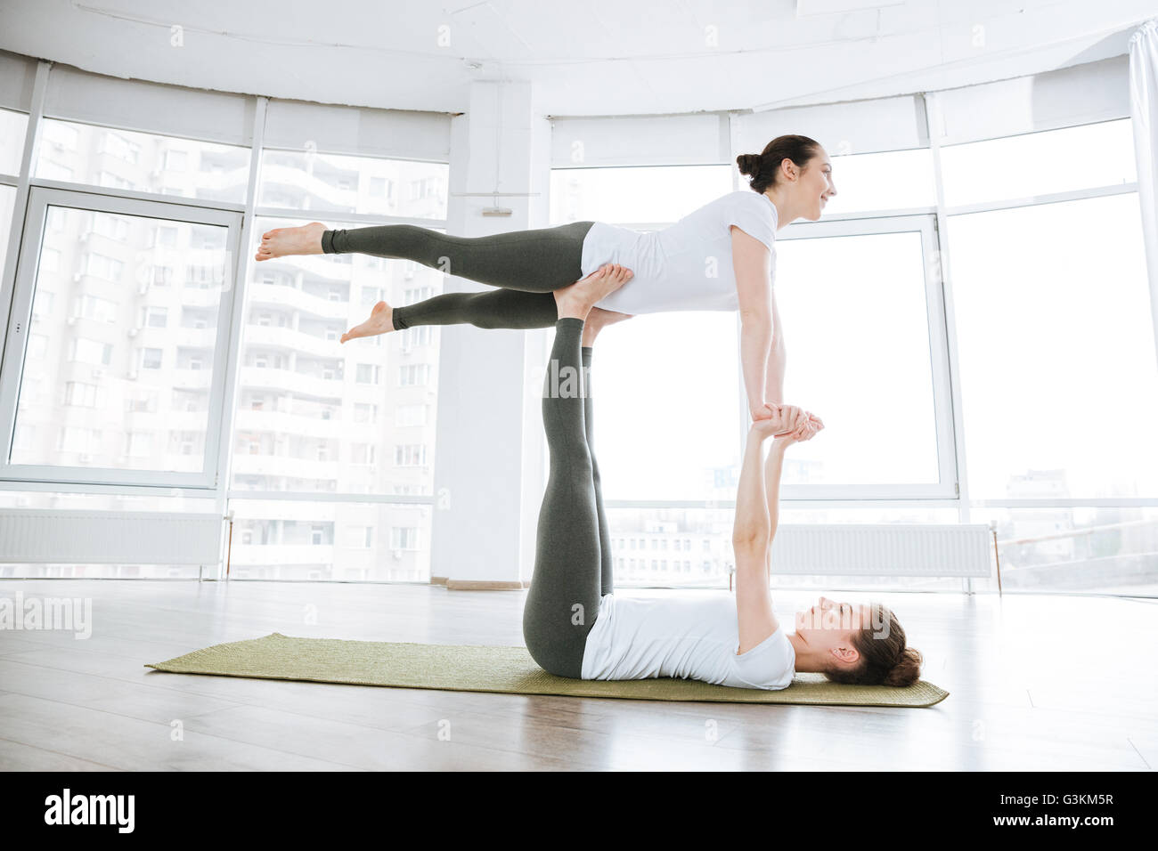 Two attractive young women balancing and doing acro yoga in studio ...