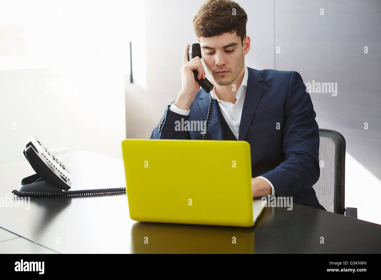 Man sitting at desk using laptop making telephone call Stock Photo - Alamy