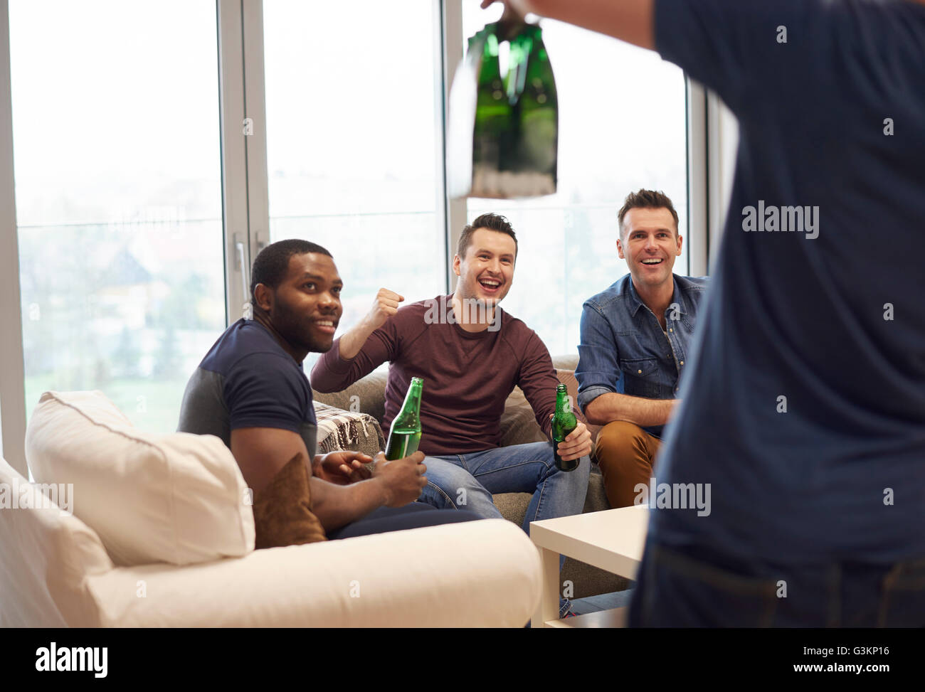 Rear view of man showing smiling friends beers Stock Photo - Alamy