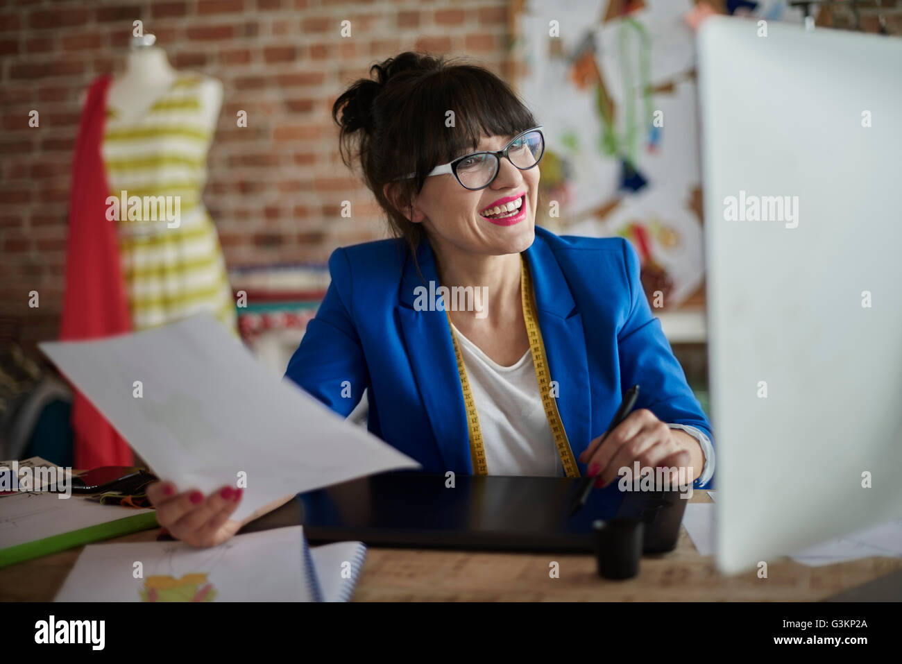 Woman in design studio holding paperwork using computerised sketch pad ...