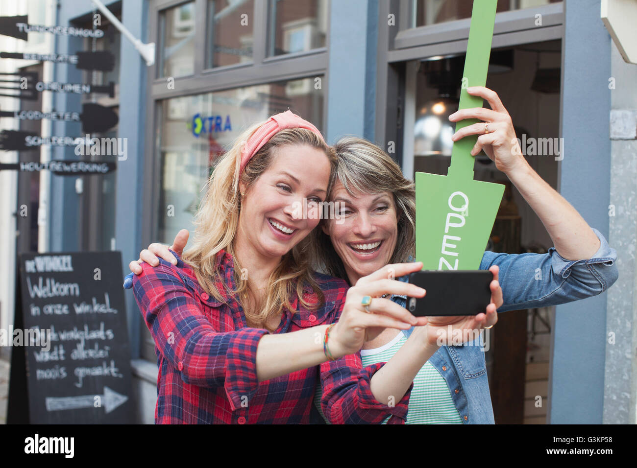 Women in front of shop holding open sign taking selfie with smartphone ...
