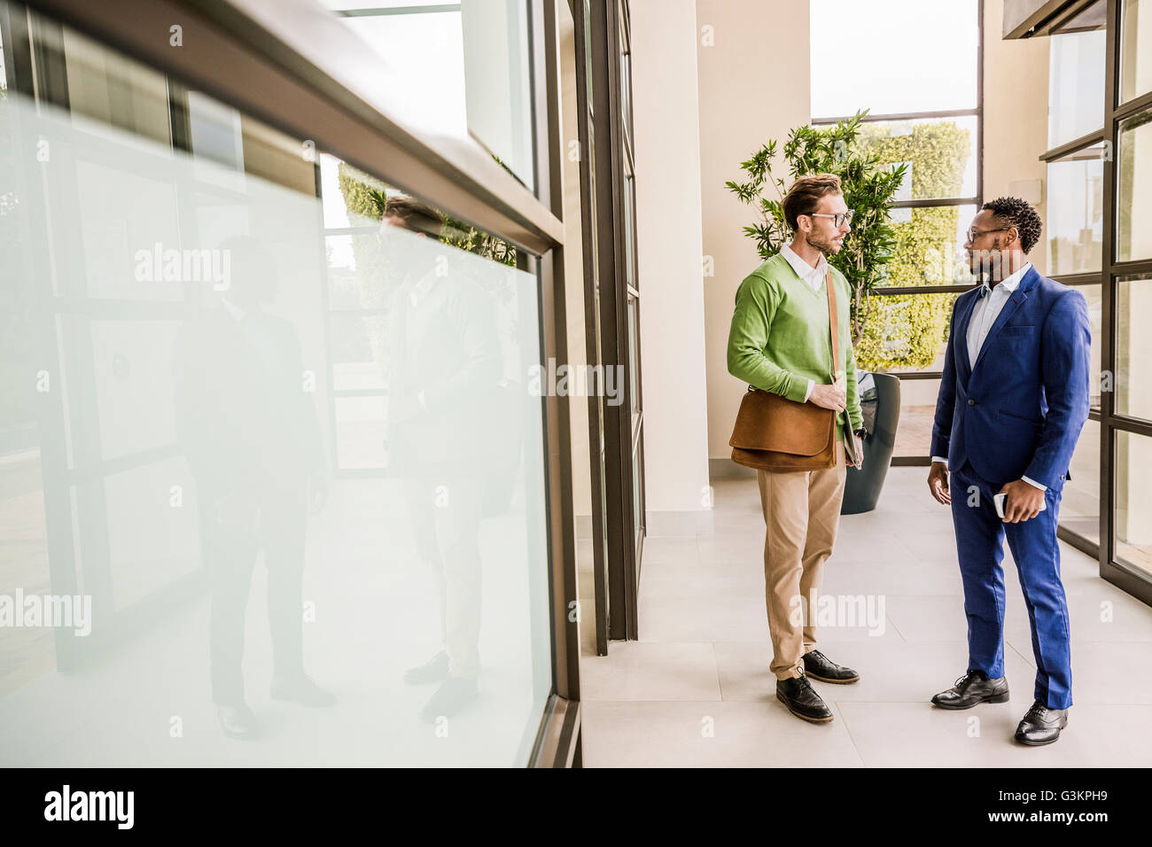 Two businessmen standing having discussion outside office building ...