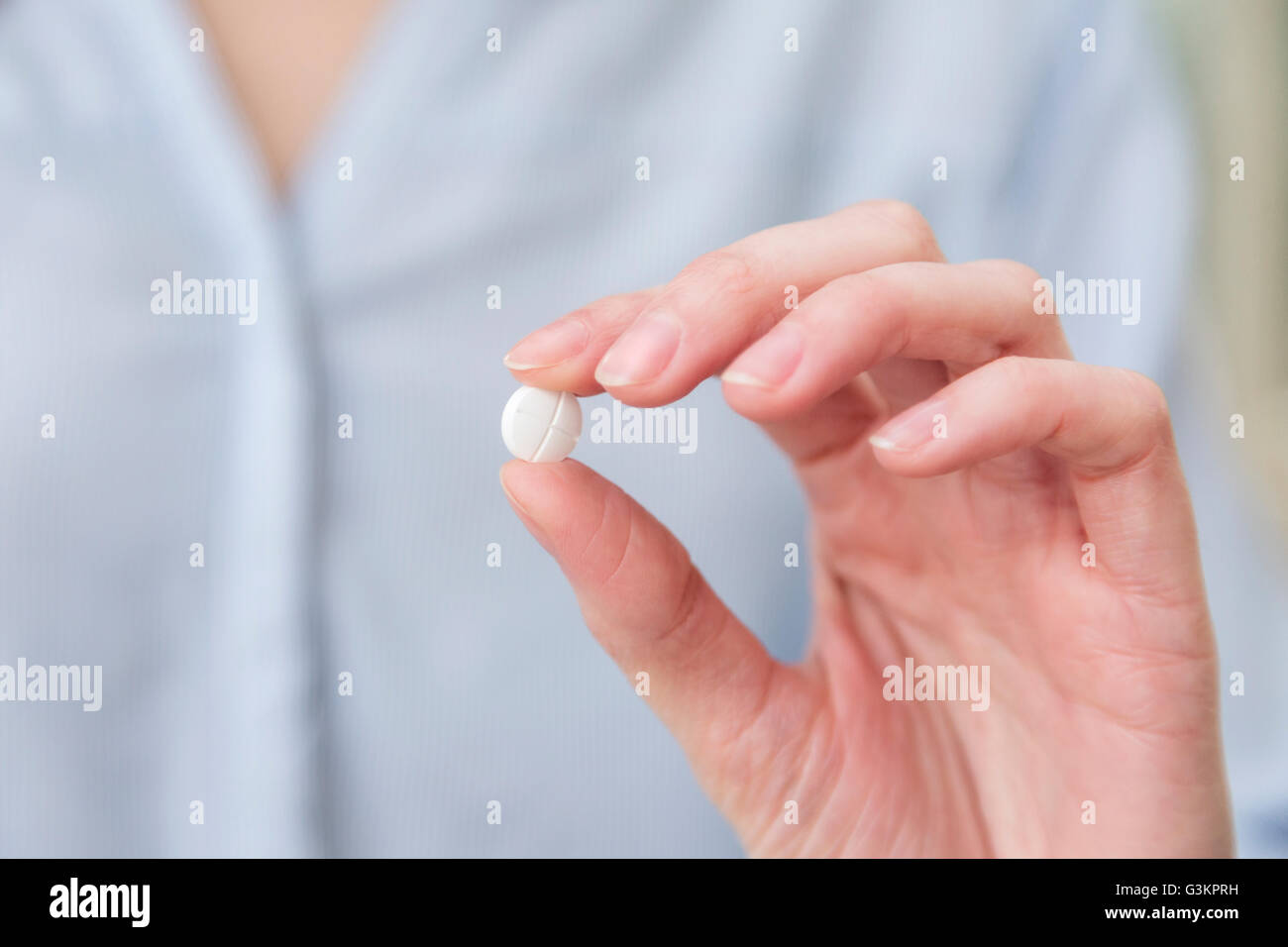 Womans hand holding pill between thumb and forefinger Stock Photo - Alamy