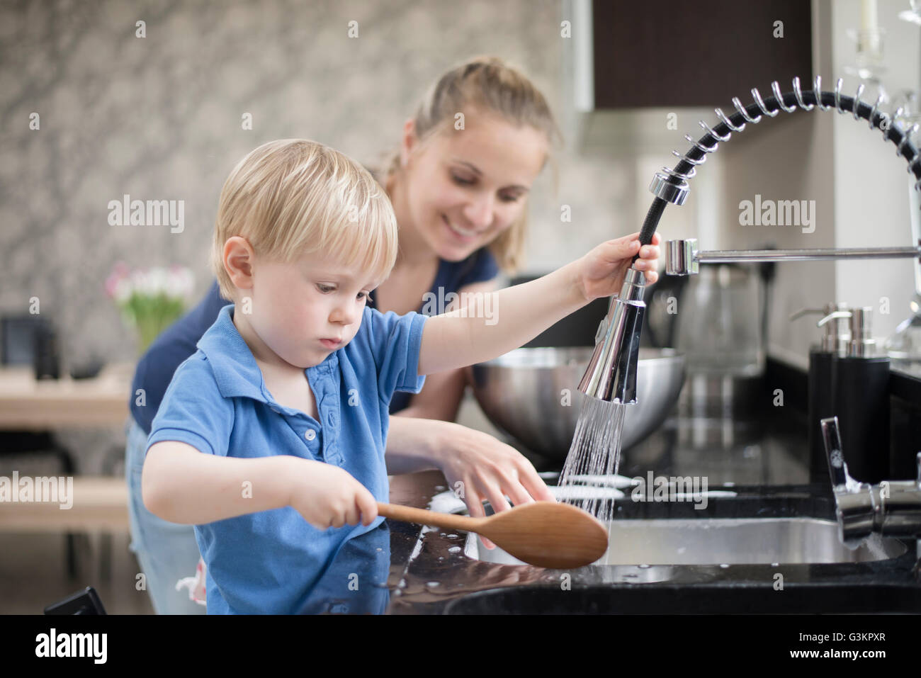 Mother helping son wash wooden spoon Stock Photo - Alamy