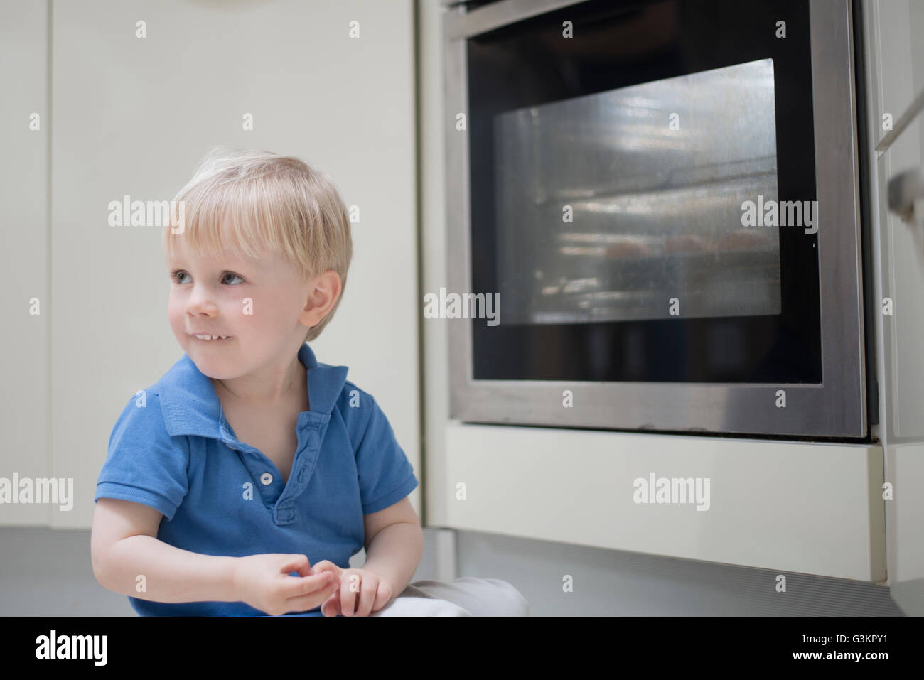 Young boy sitting on floor in kitchen, beside oven Stock Photo - Alamy