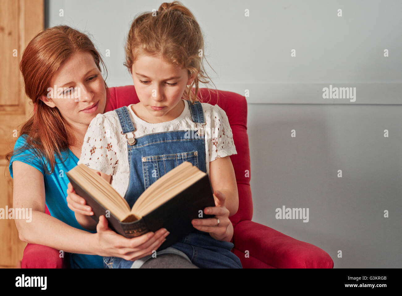 Mid adult woman reading book with daughter on armchair Stock Photo - Alamy