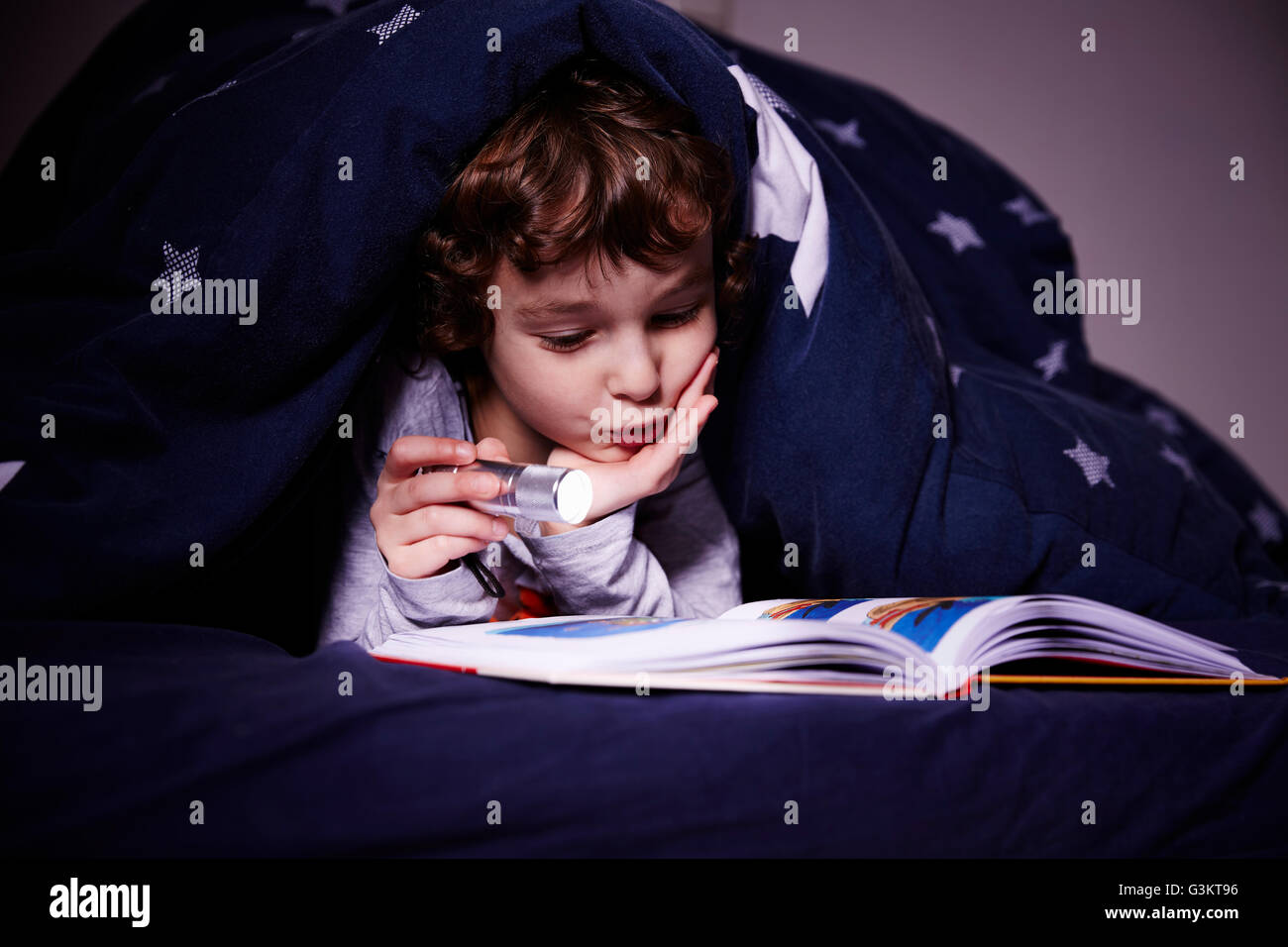 Boy underneath duvet reading book by torchlight Stock Photo - Alamy
