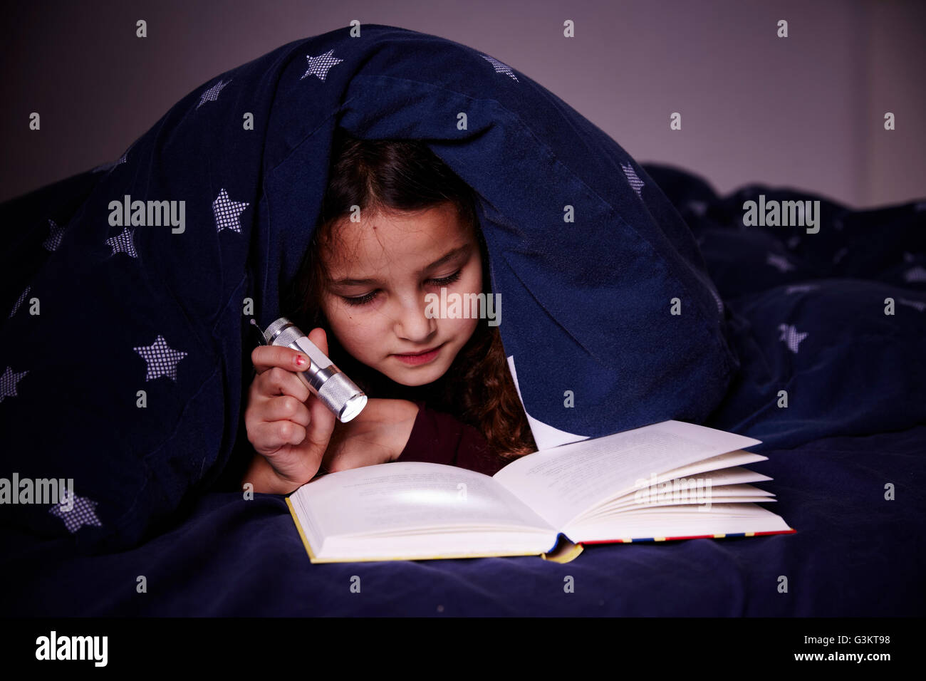 Girl underneath duvet reading book by torchlight Stock Photo - Alamy