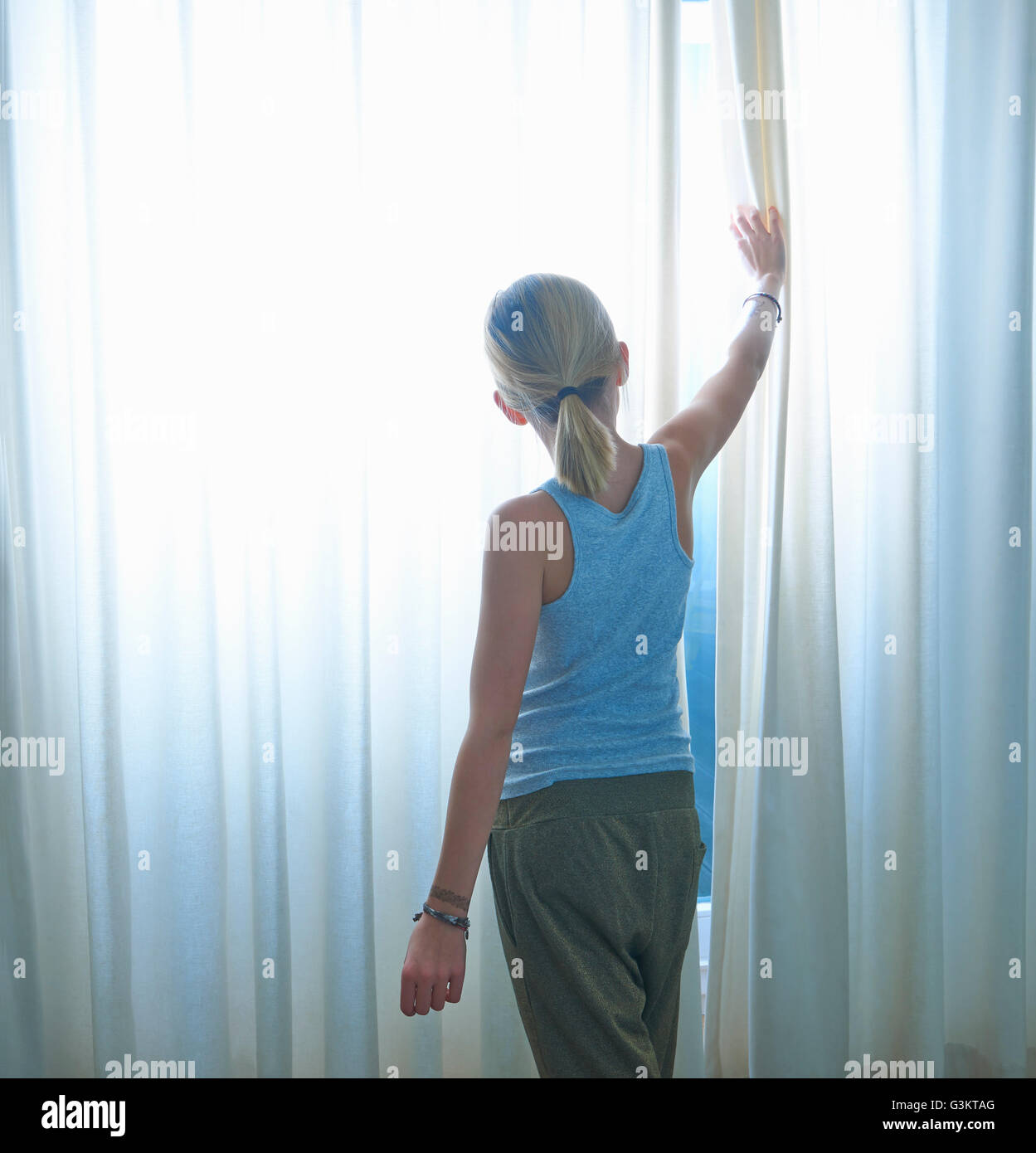 Rear view of girl peering through net curtained window Stock Photo - Alamy