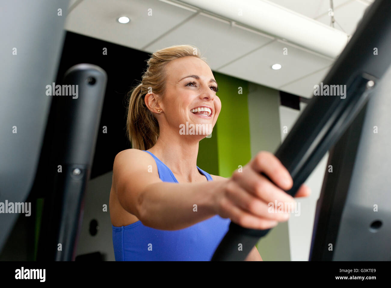 Woman in gym using exercise machine smiling Stock Photo - Alamy