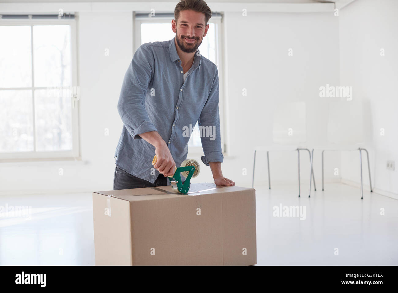 Portrait of young man taping cardboard box whilst moving house Stock ...