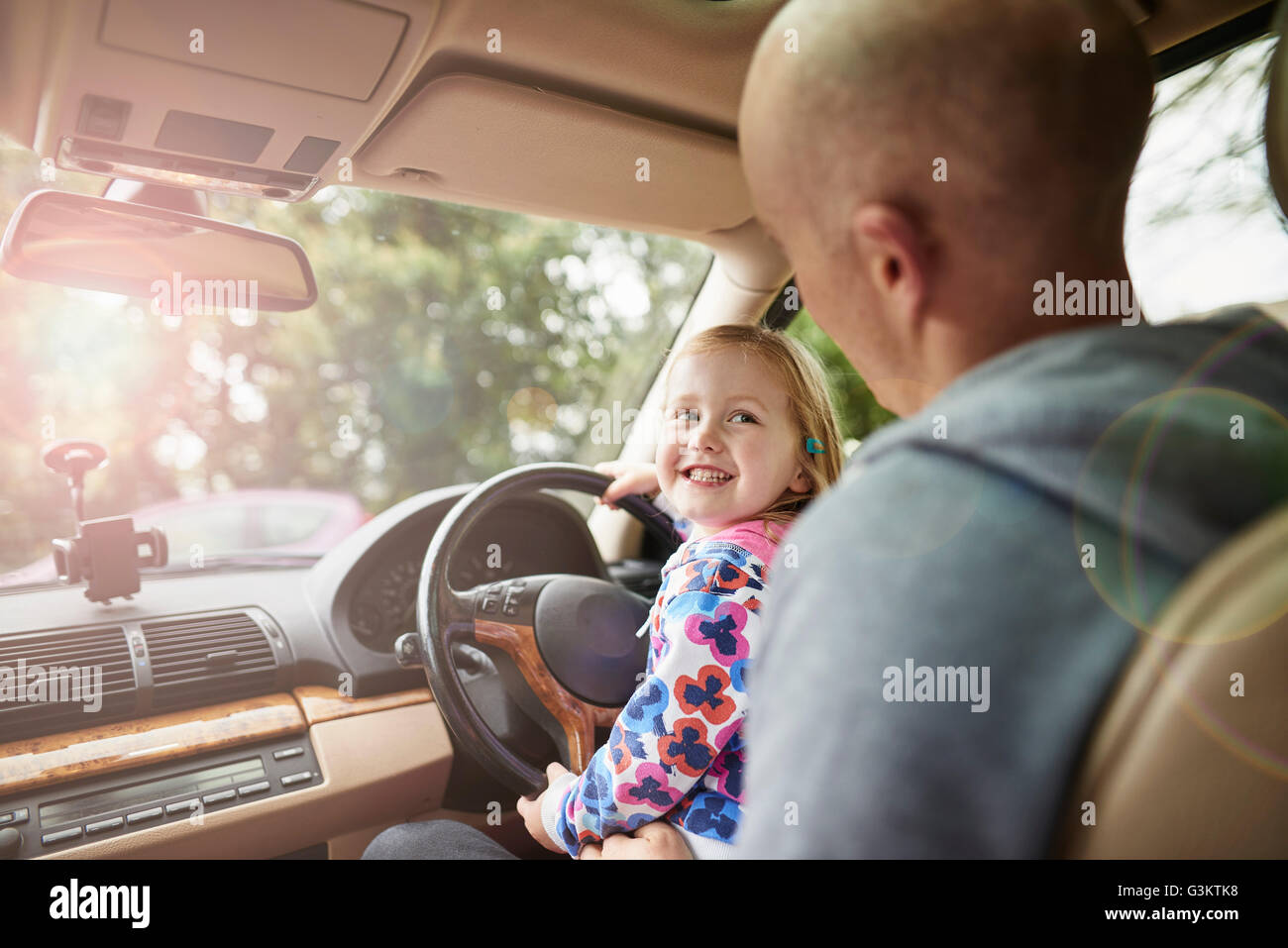 Over shoulder view of daughter sitting on father lap driving car Stock ...
