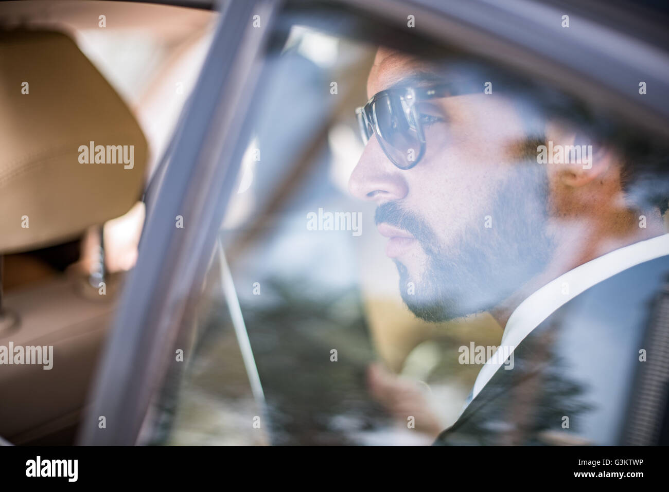 Young businessman wearing sunglasses looking out of car window from ...