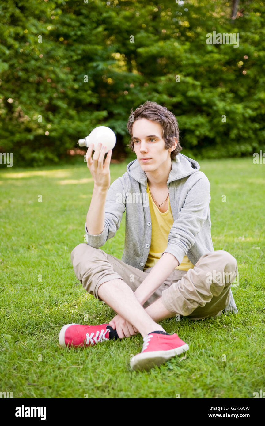 Young man sitting in nature, holding lightbulb Stock Photo - Alamy