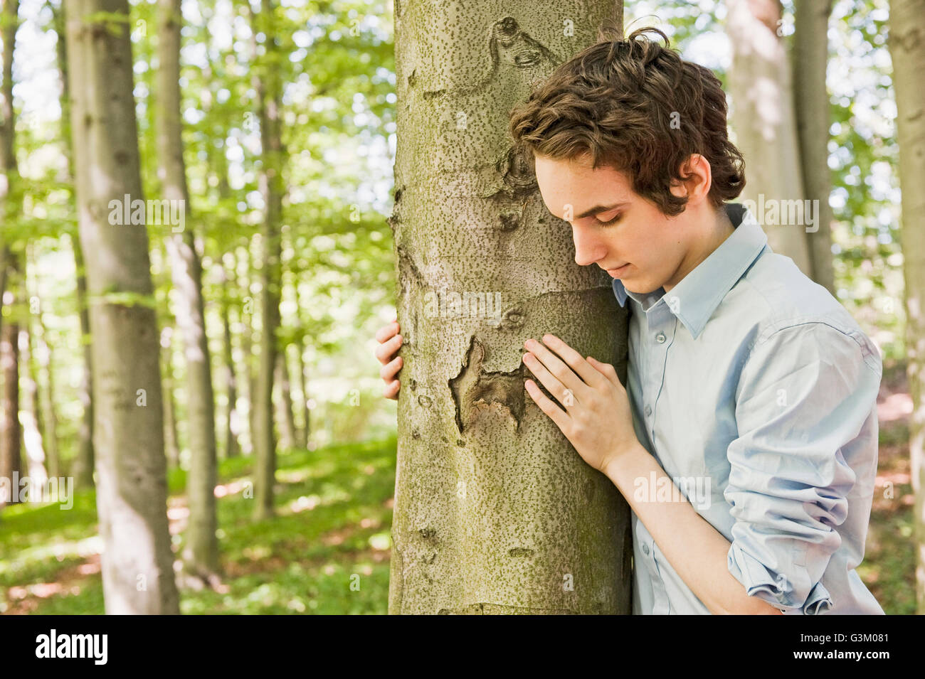Young man standing by a tree in the woods Stock Photo - Alamy