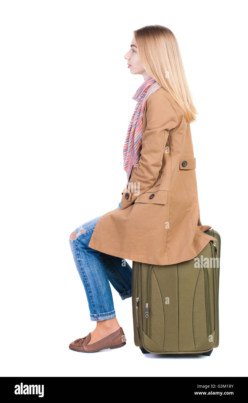 back view of woman in cloak sits on a suitcase. beautiful girl in ...