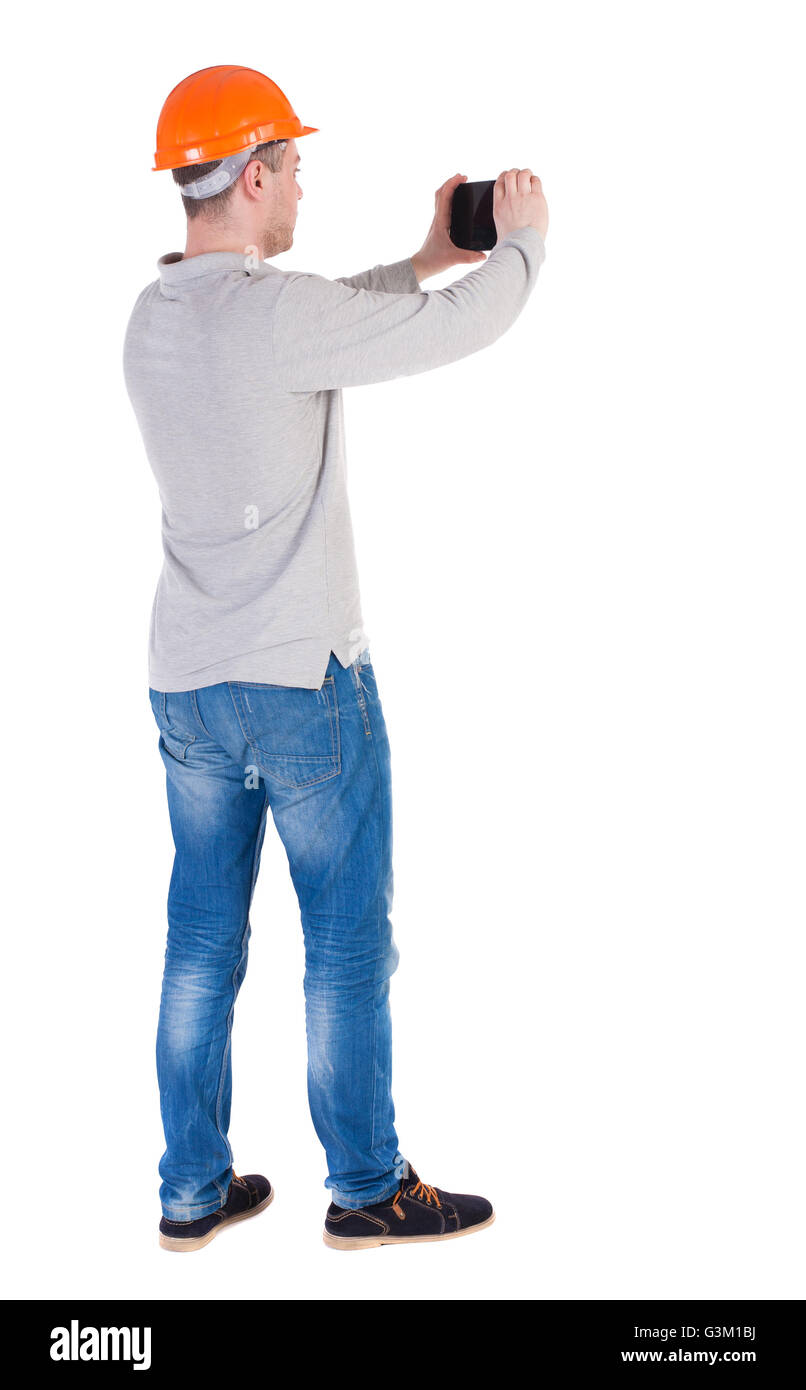 Backview of an engineer in construction helmet stands and enjoys tablet ...
