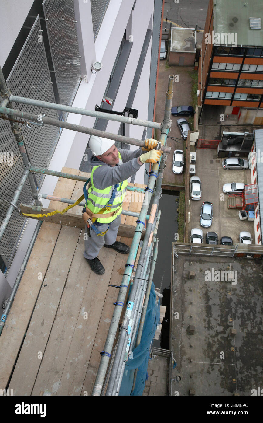 A scaffolder builds a temporary work platform near the top of a tall ...