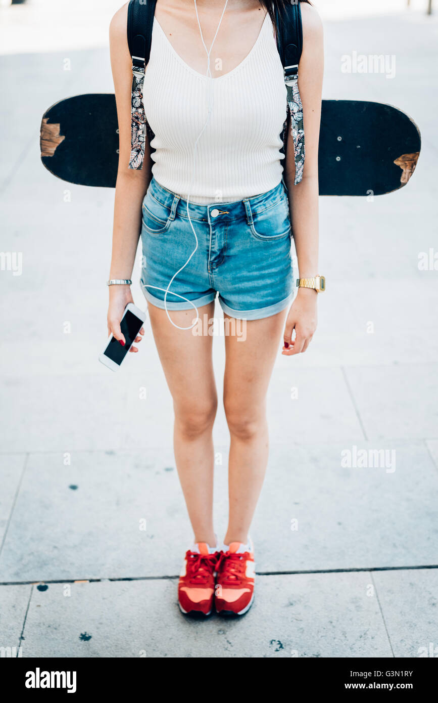 From the neck down view of young woman with skateboard and backpack ...