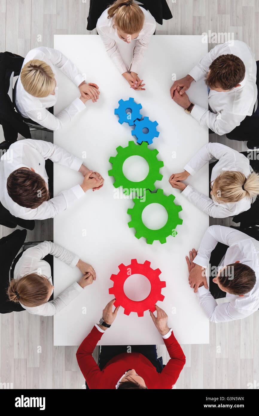 Business team sitting around the table with cogs, teamwork concept ...