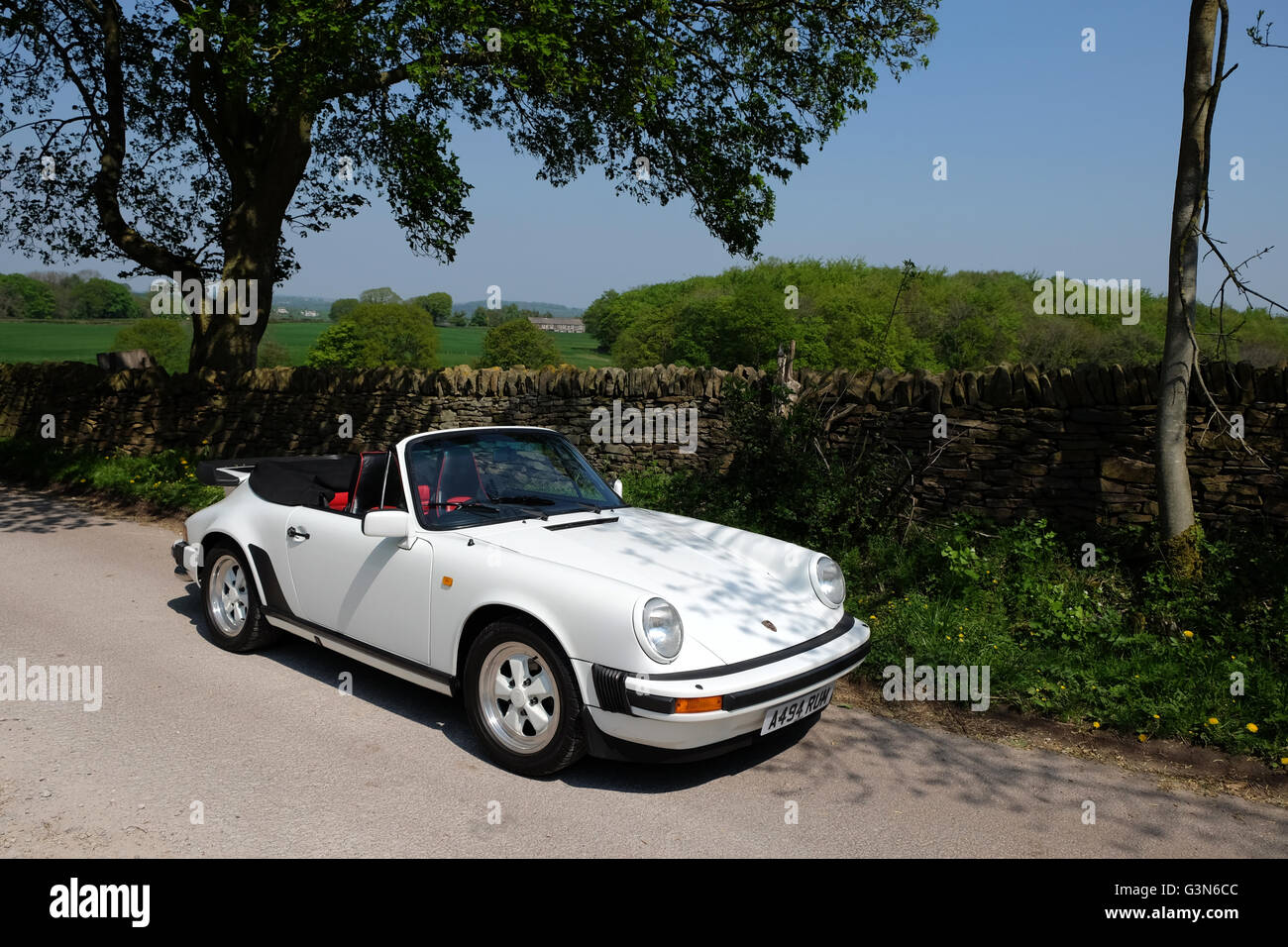 Porsche 911 cabriolet parked in the shade of a tree and a dry tone wall ...