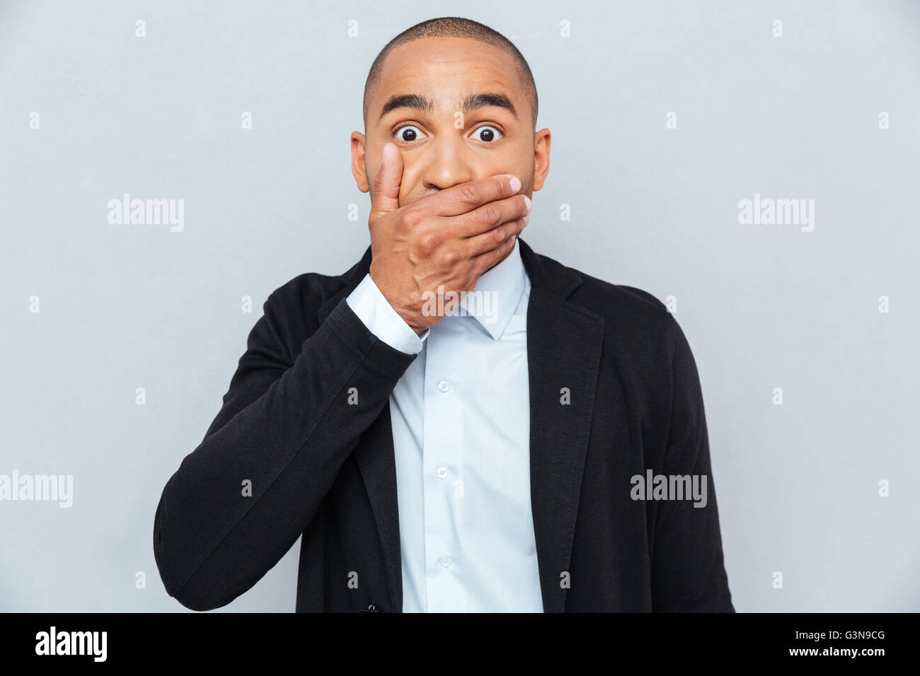 Handsome young african man covering mouth with hand isolated on gray ...