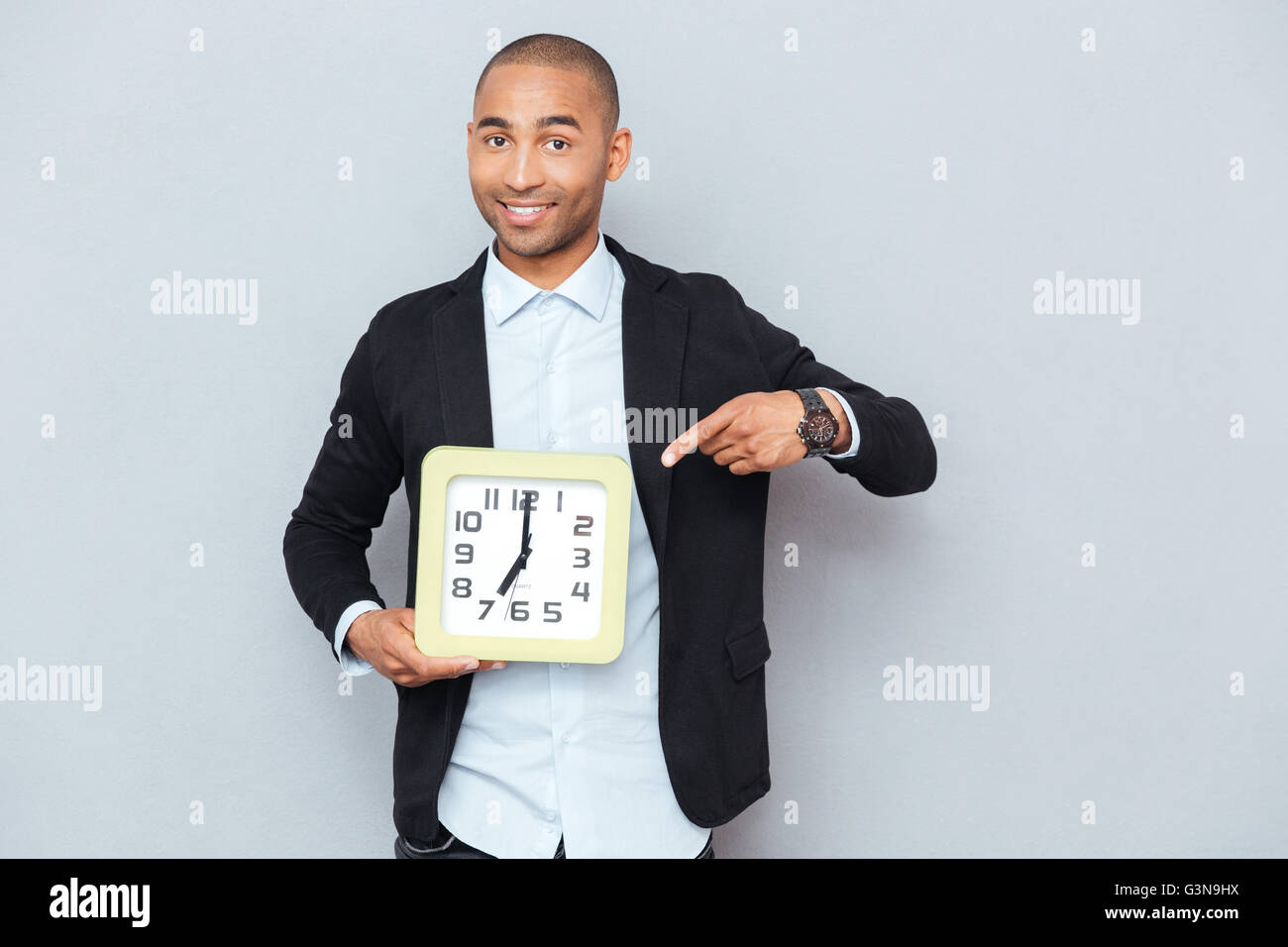 Happy african american young man holding clock anf pointing on it Stock ...