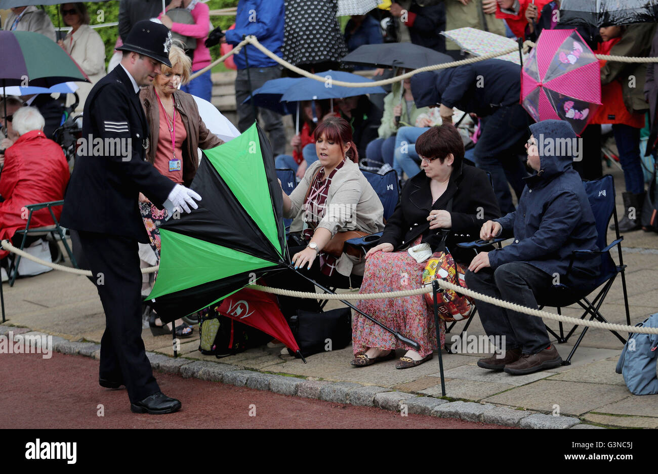 A police officer helps a spectator with her umbrella as members of the ...