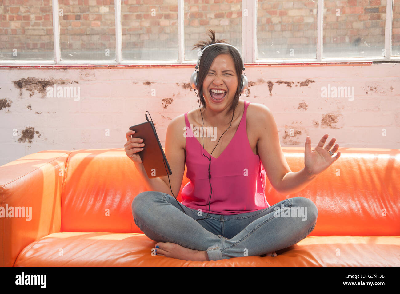 woman sitting crossed legged on a sofa listening to music on headphones ...