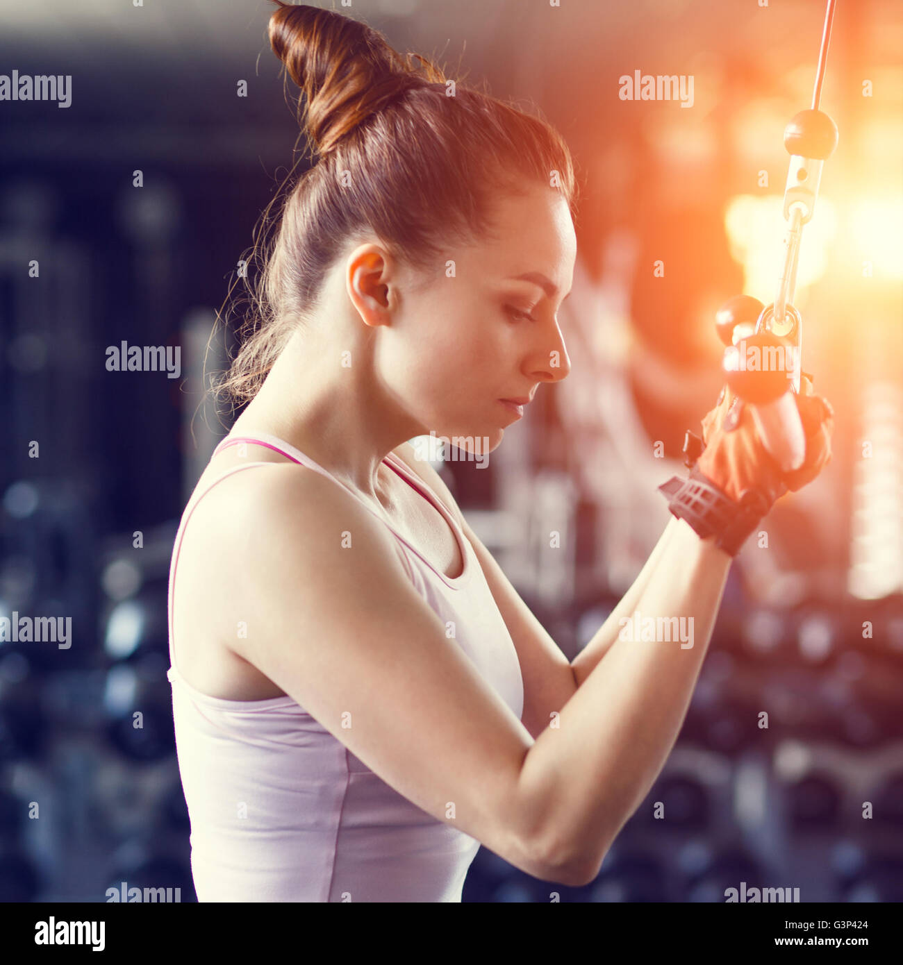 Young slim woman doing pushdown on cable machine in gym in sunset beams ...