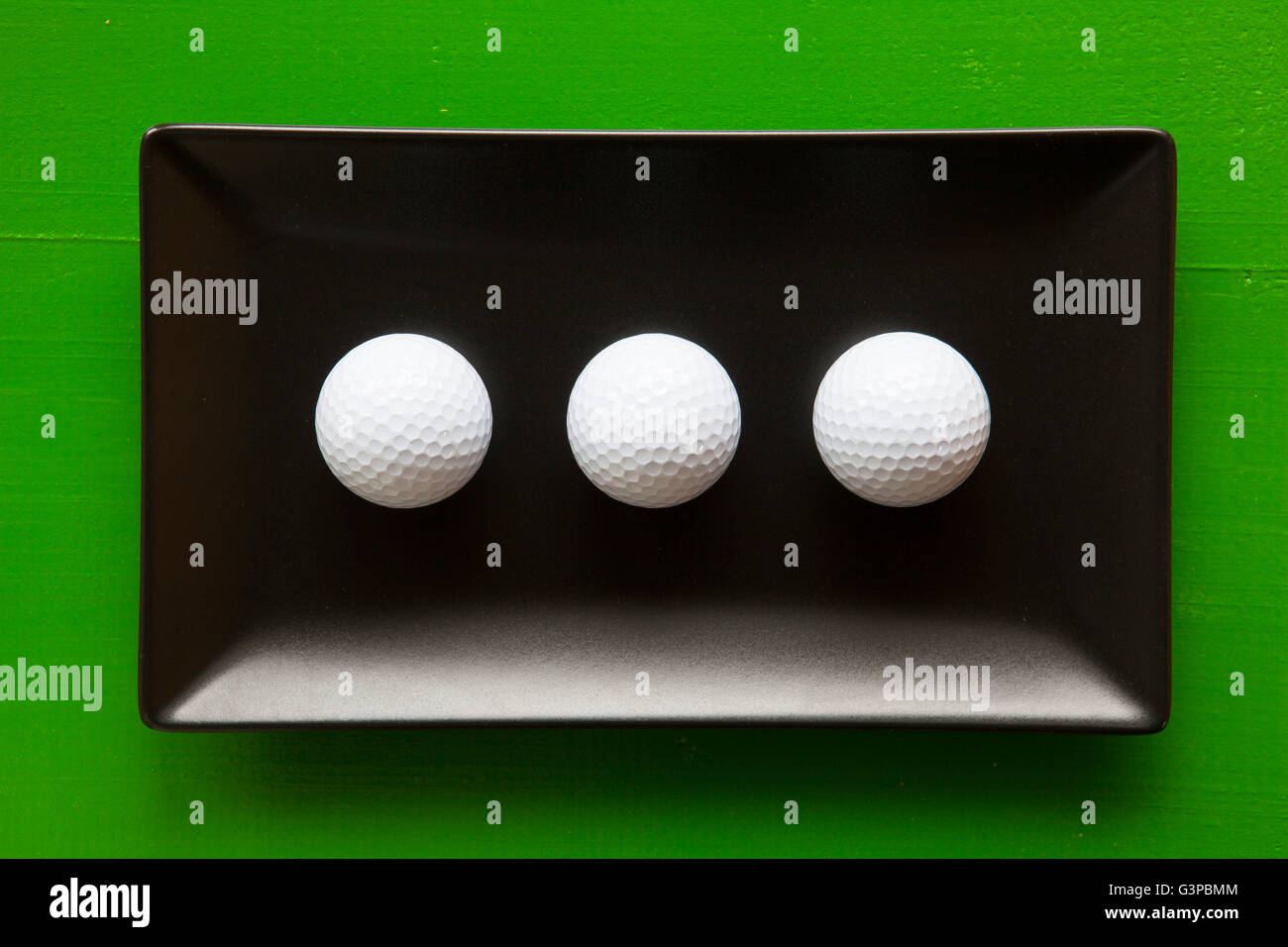 Black ceramic dishes with golf balls on over green background ...