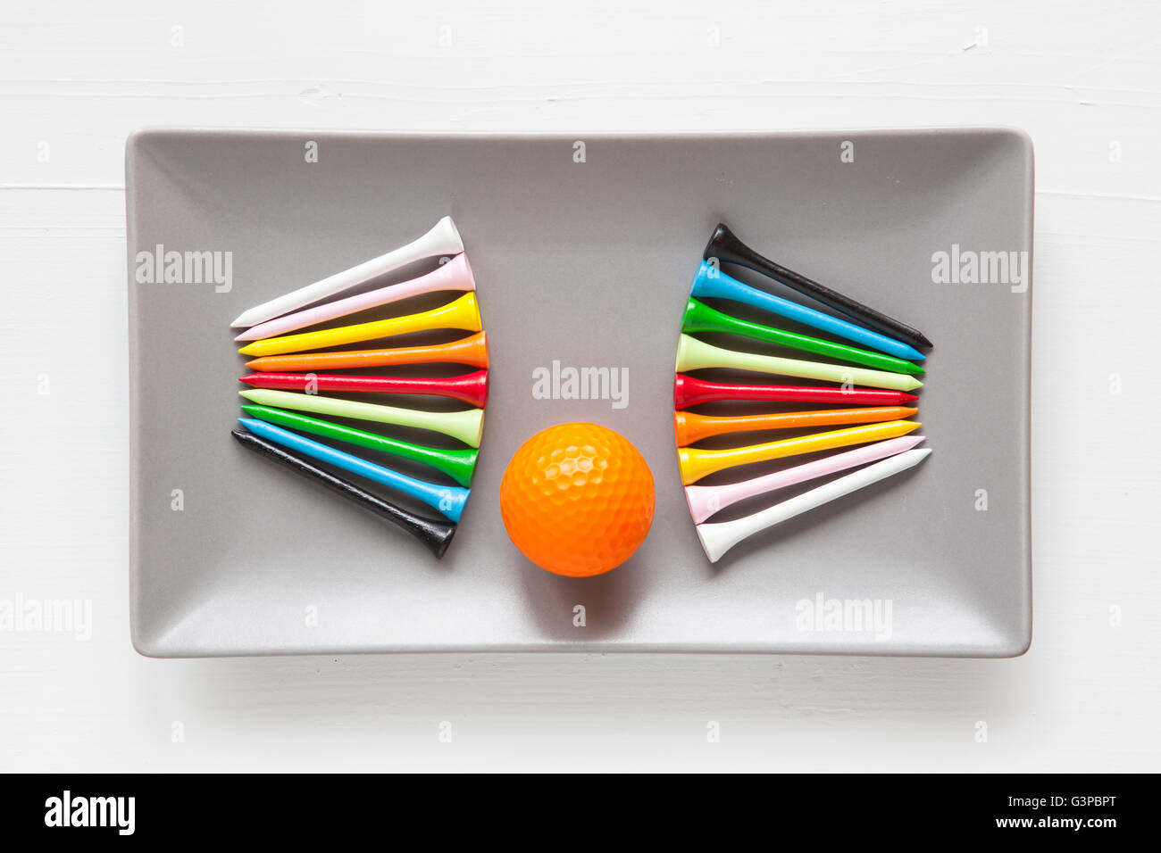 Gray ceramic dishes with golf balls and wooden tees on over white ...