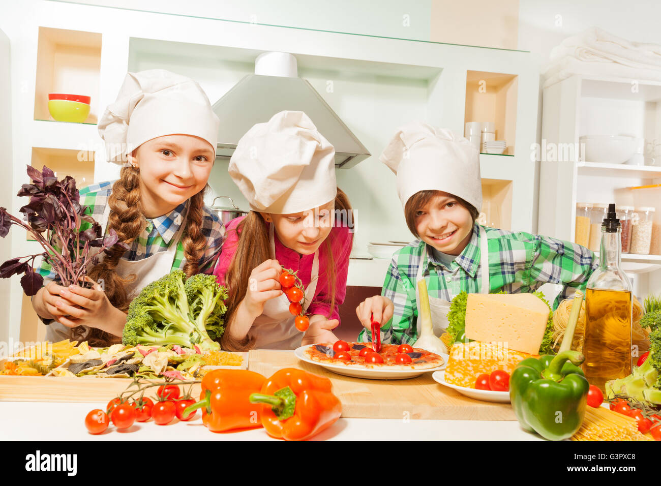 Three young cooks cutting pizza at the kitchen Stock Photo - Alamy