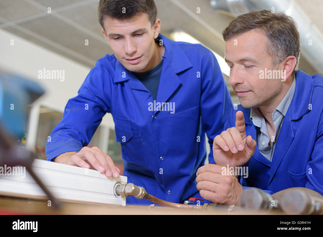 Plumber and appretice with radiator on workbench Stock Photo - Alamy