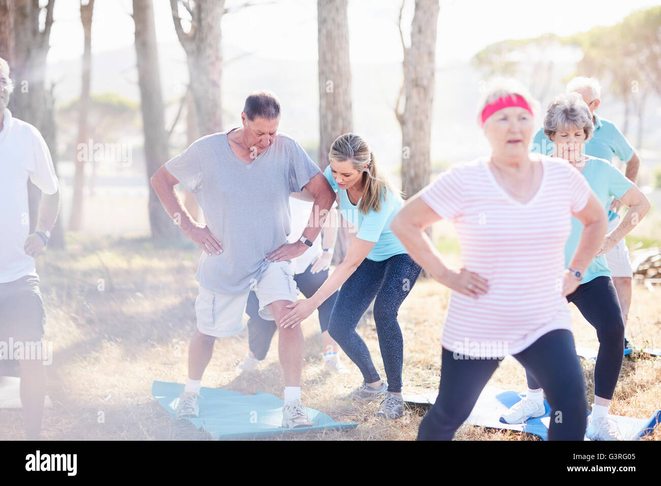 Yoga instructor guiding senior man in sunny park Stock Photo - Alamy