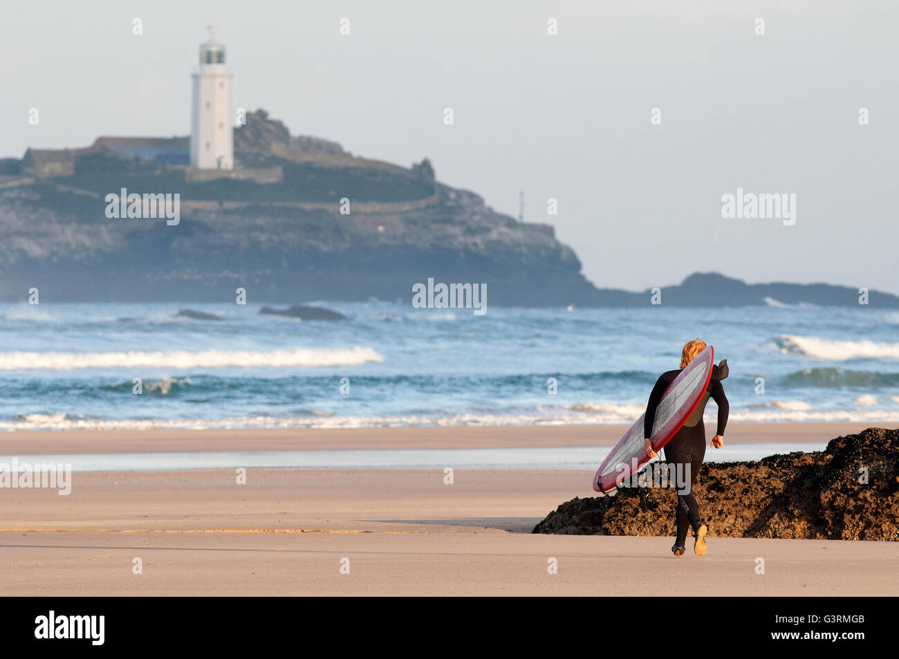 Surfer with red and white surfboard running down the sand to the waves ...