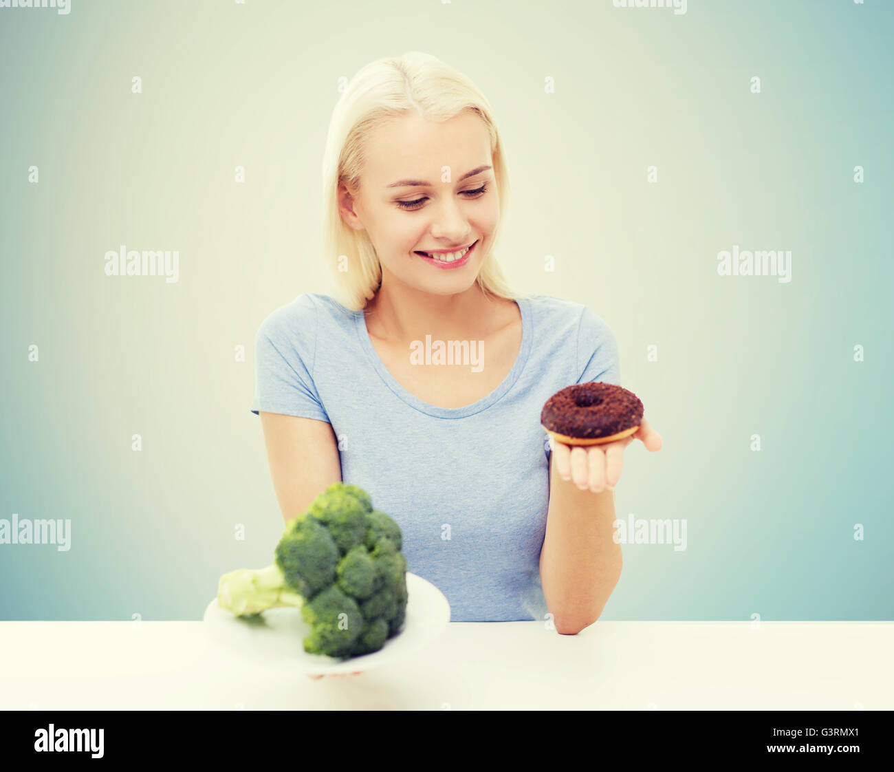 smiling woman choosing between broccoli and donut Stock Photo - Alamy