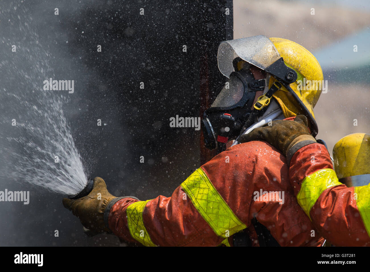 fireman in helmet and oxygen mask spraying water to fire surround with ...