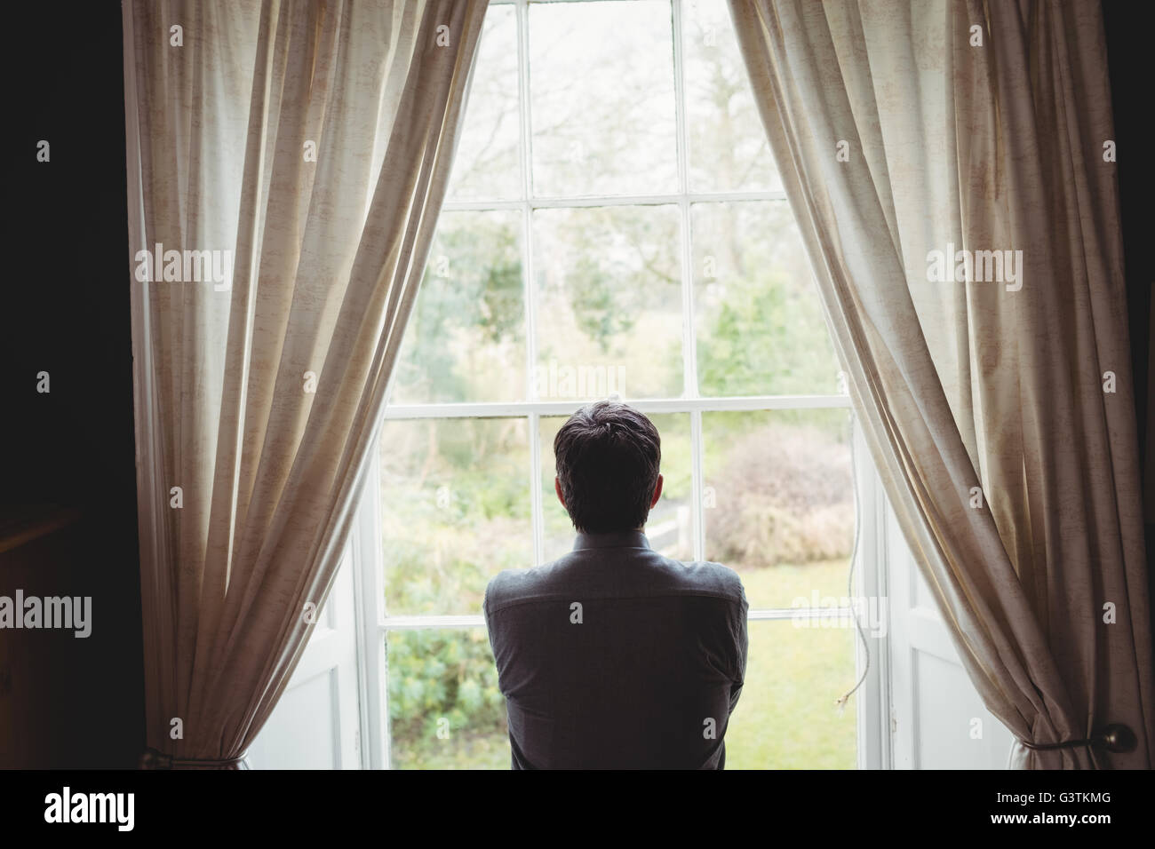 Rear view of mature man looking through window Stock Photo - Alamy